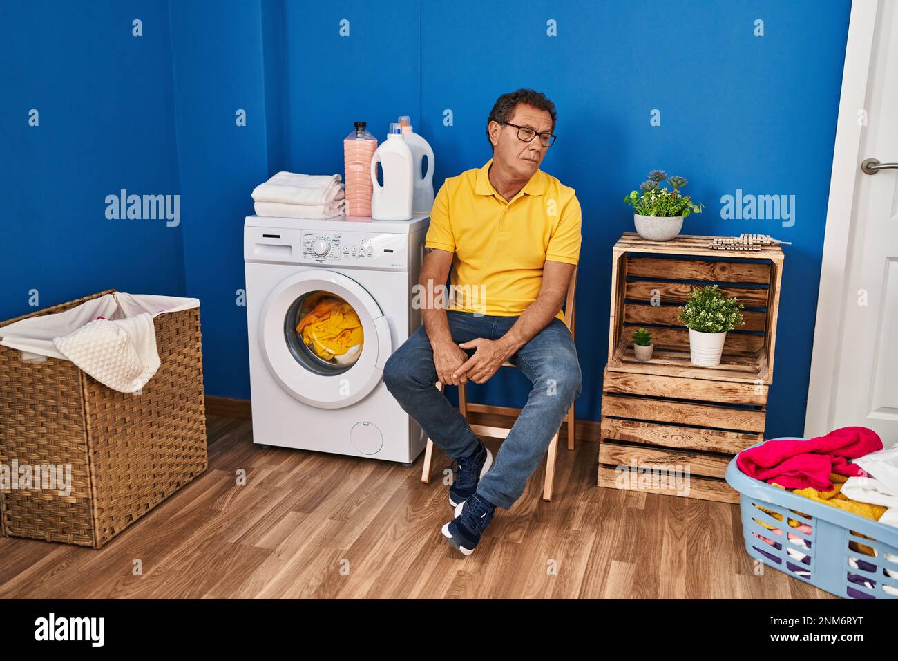 Middle age man sitting on chair waiting for washing machine at laundry ...