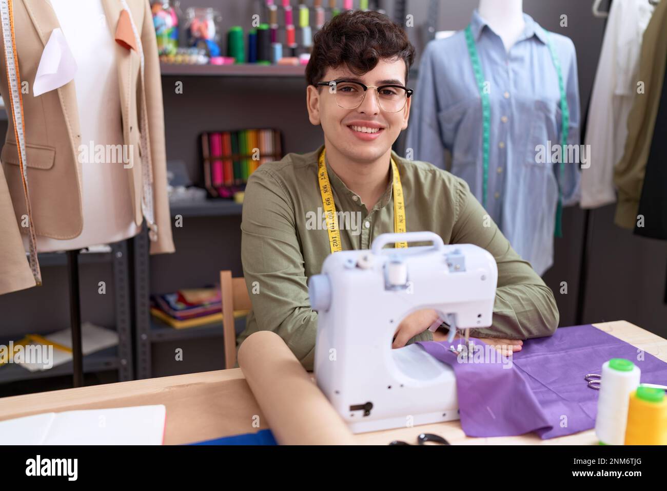 Non binary man tailor smiling confident using sewing machine at atelier ...