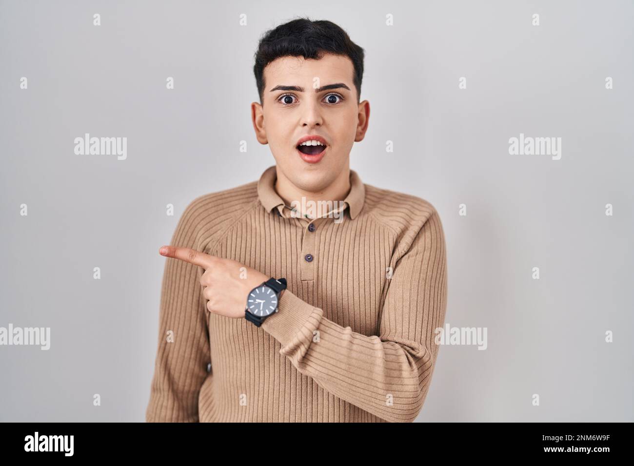 Non binary person standing over isolated background surprised pointing ...