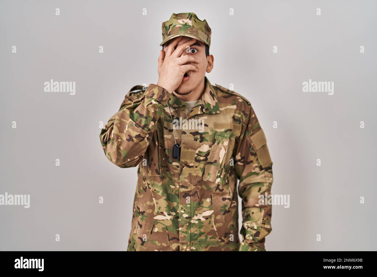 Young arab man wearing camouflage army uniform peeking in shock ...