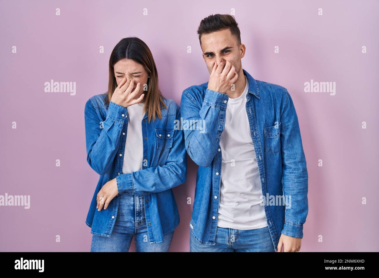 Young hispanic couple standing over pink background smelling something ...