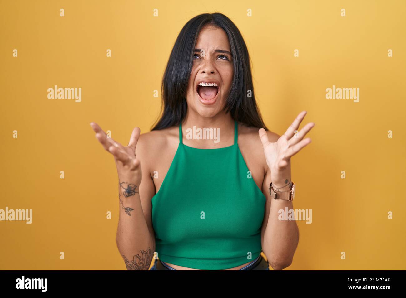 Brunette woman standing over yellow background crazy and mad shouting ...