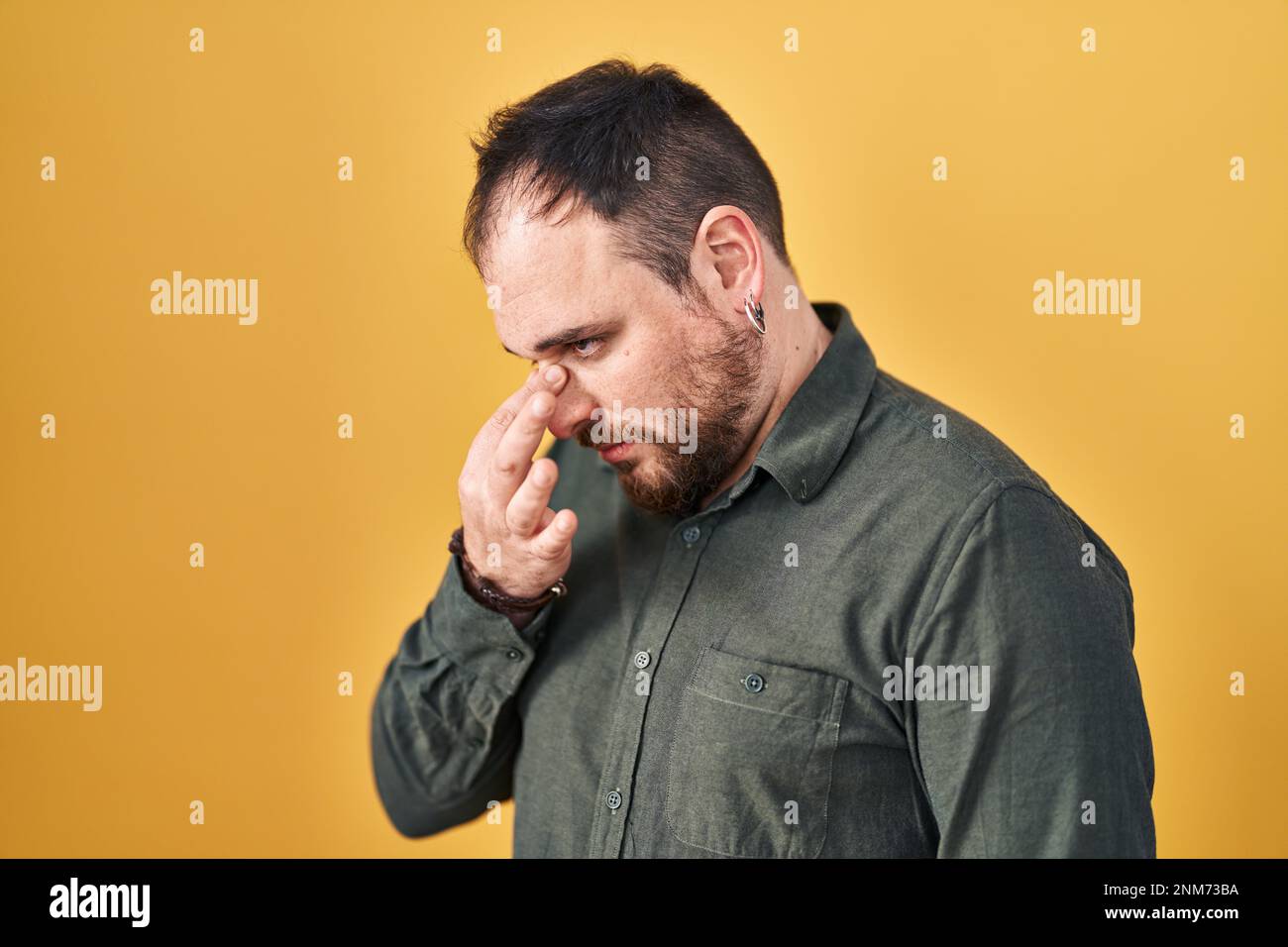 Plus size hispanic man with beard standing over yellow background tired ...