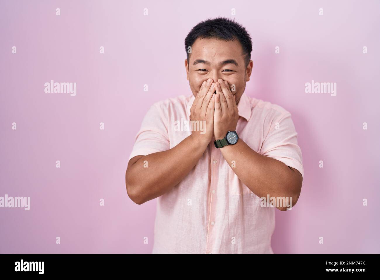 Chinese young man standing over pink background laughing and ...