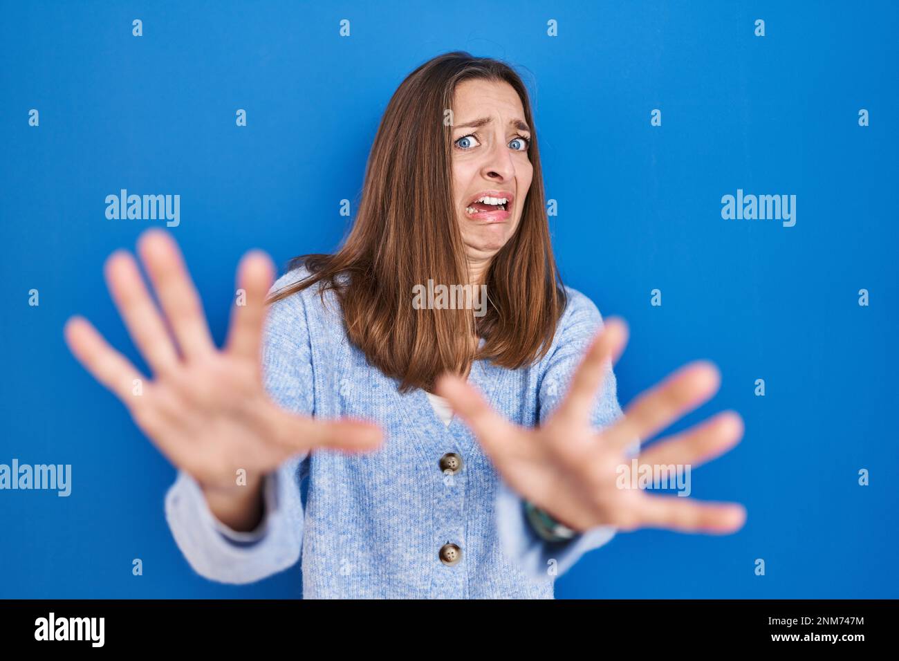 Young woman standing over blue background afraid and terrified with ...