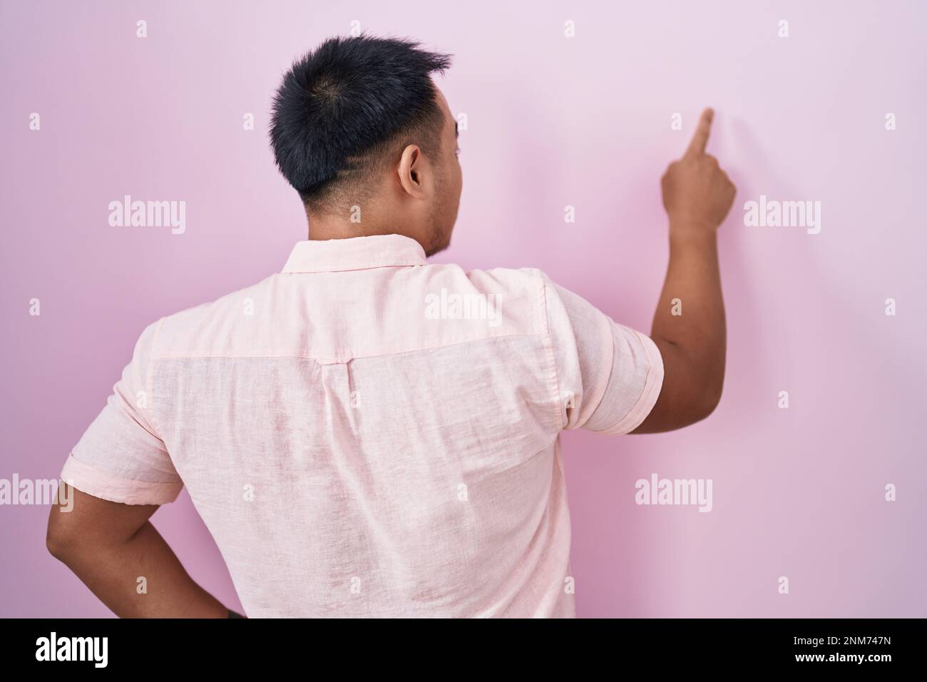 Chinese young man standing over pink background posing backwards ...