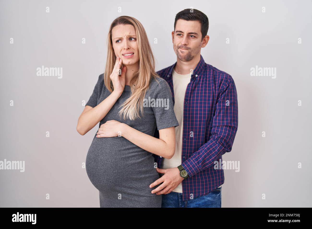 Young couple expecting a baby standing over white background touching ...
