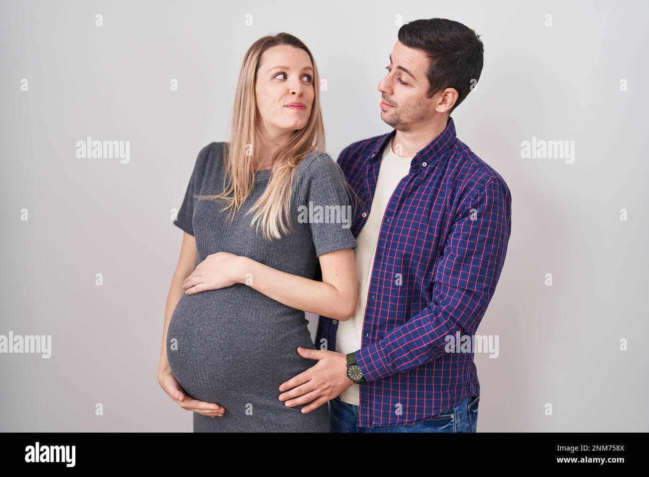 Young couple expecting a baby standing over white background smiling ...