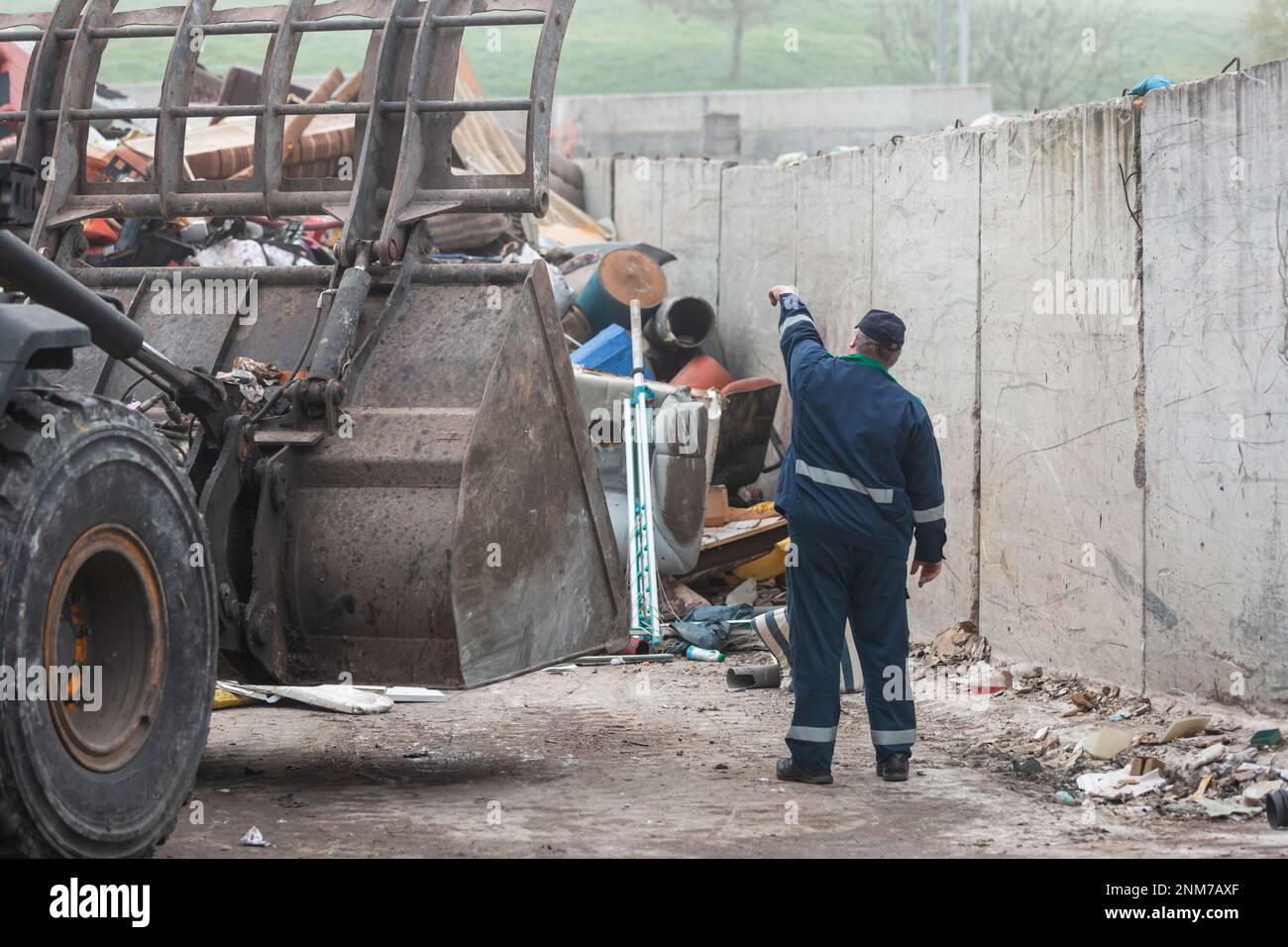 Worker at a recycling center standing near a bucket loader, looking and ...