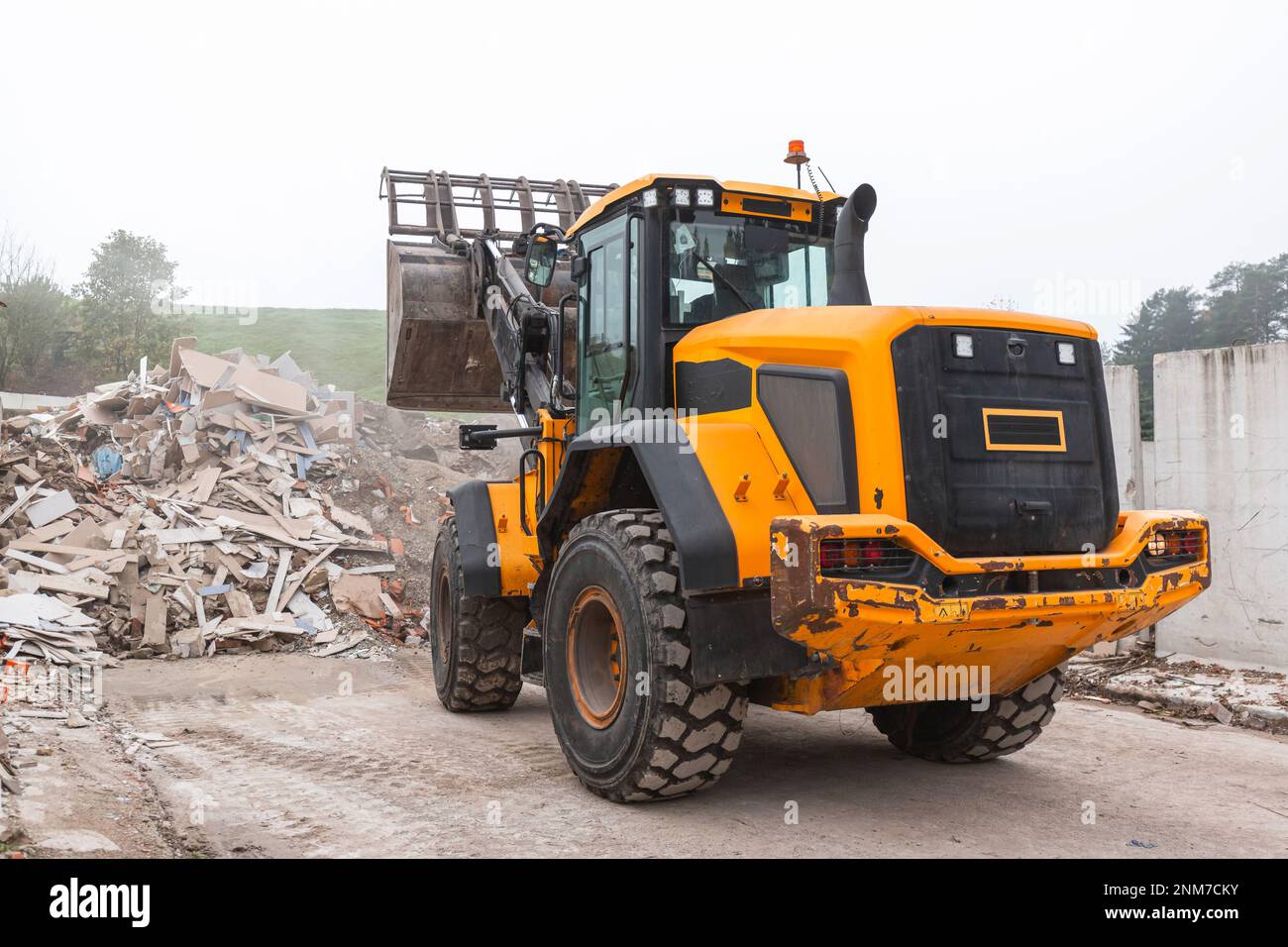 Yellow wheel loader, with lifted scrap grapple, moving along the ...