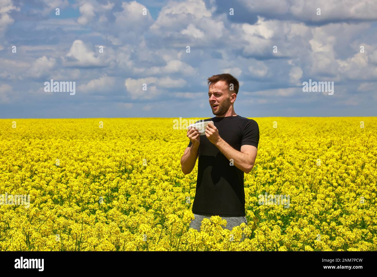 Young man in yellow canola field blowing his nose and suffering from ...