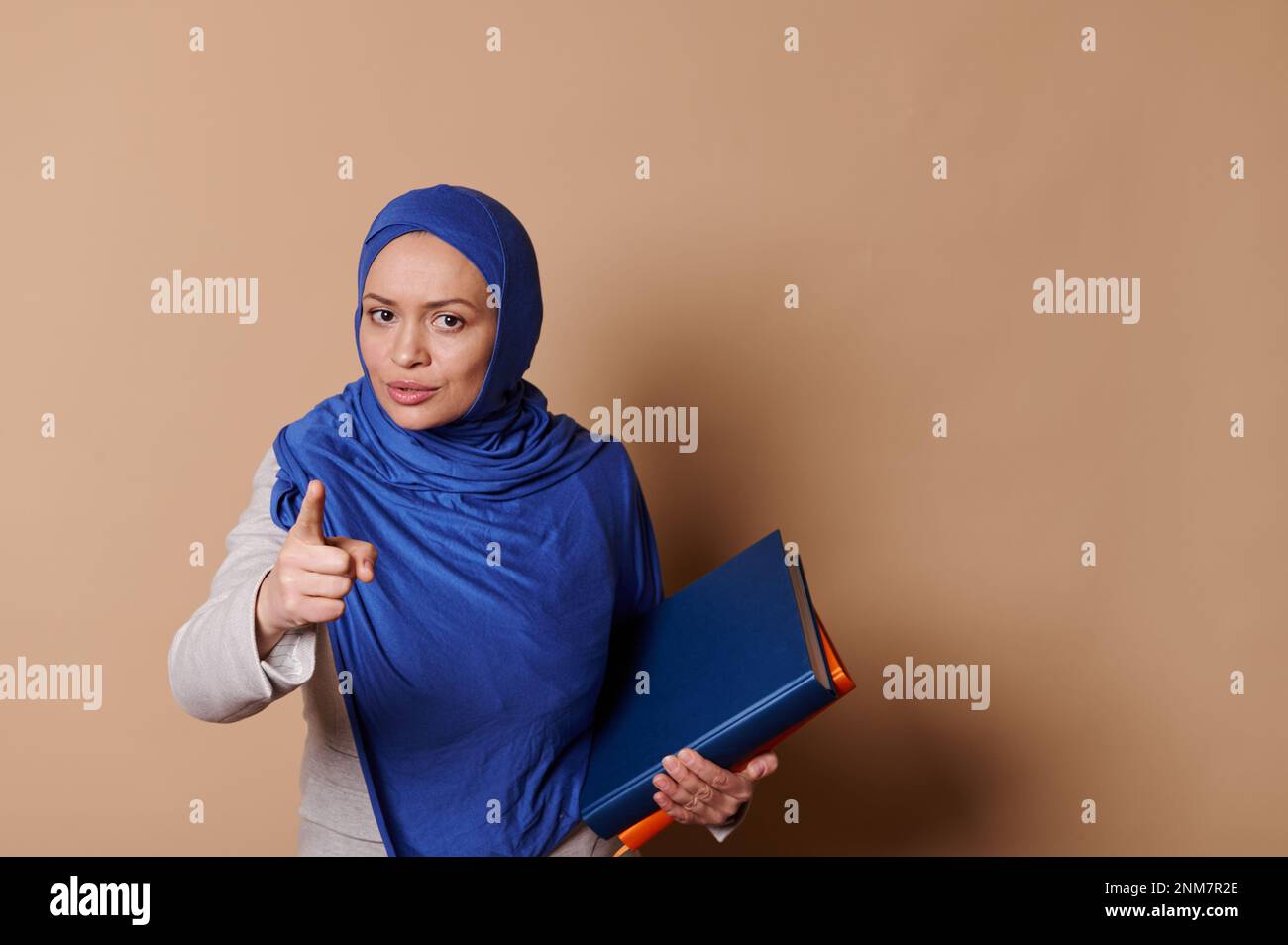 Strict Arab Muslim woman in hijab, holding books and pointing at camera ...