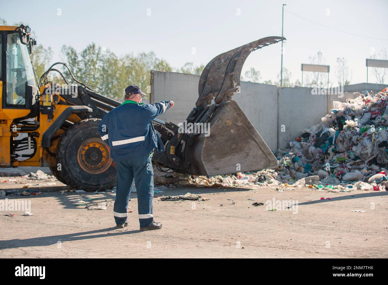 Landfill worker directing skid steer loader on the garbage heap, rear ...
