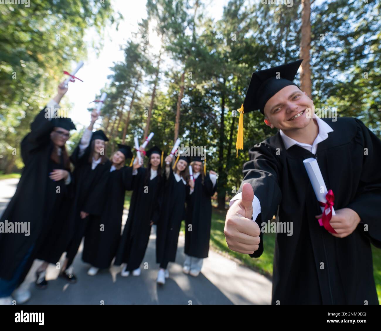 Happy young caucasian male graduate showing thumbs up. A group of ...