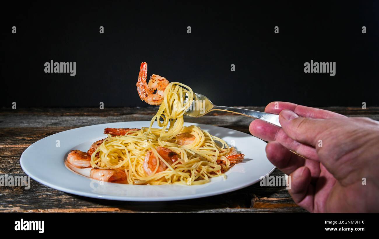 Spaghetti with shrimps on fork in mans had with black background and ...