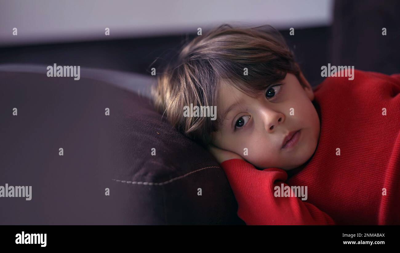 Closeup little boy face lying on sofa watching cartoon. Child ...