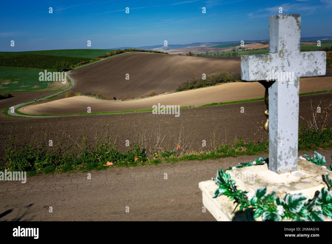 A standing stone wayside cross overlooking wavy Moravian fields with an ...