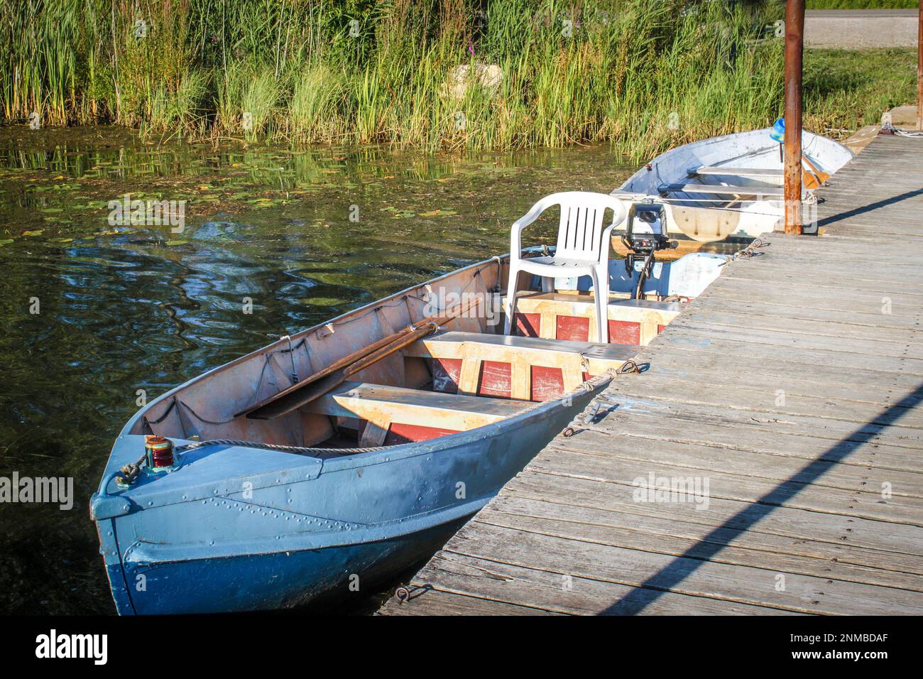 Metal row boats - one with plastic chair in it- pulled up to pier with ...