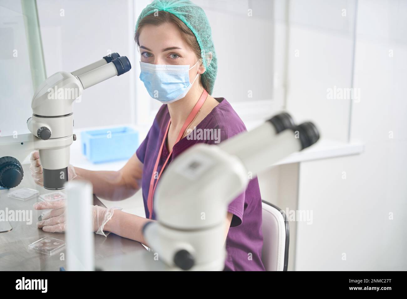 Young laboratory worker is at her workplace at powerful microscope ...