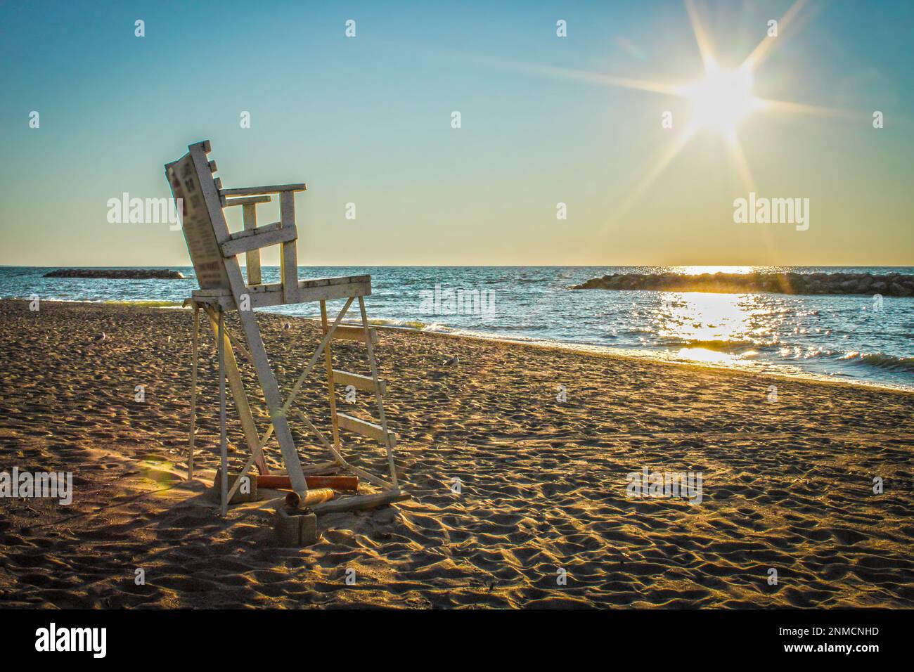 Wooden abandoned lifeguard chair on beach with sunspot in the sky ...