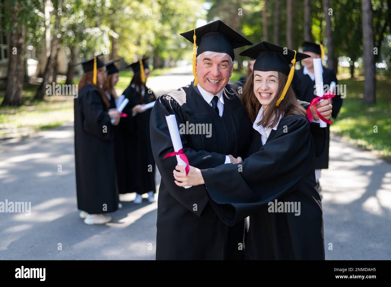 A group of graduates in robes outdoors. An elderly man and a young ...