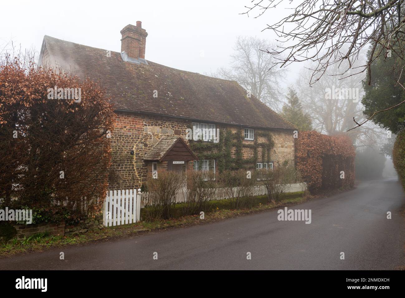 A brick and stone cottage in the village of Graffham on a foggy winter ...