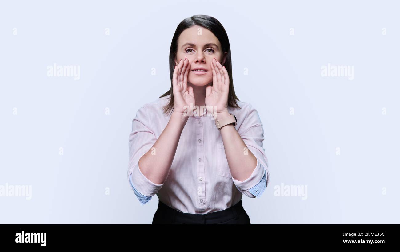 Young woman telling secret, holding her hands near her lips, on white ...