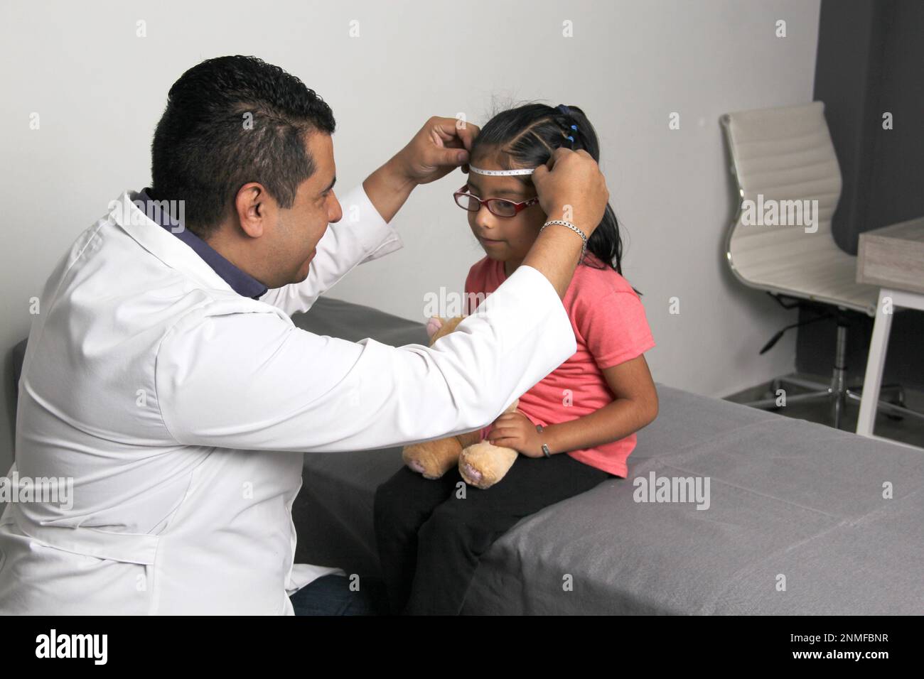 Latino pediatrician doctor checks his girl patient with autism spectrum ...
