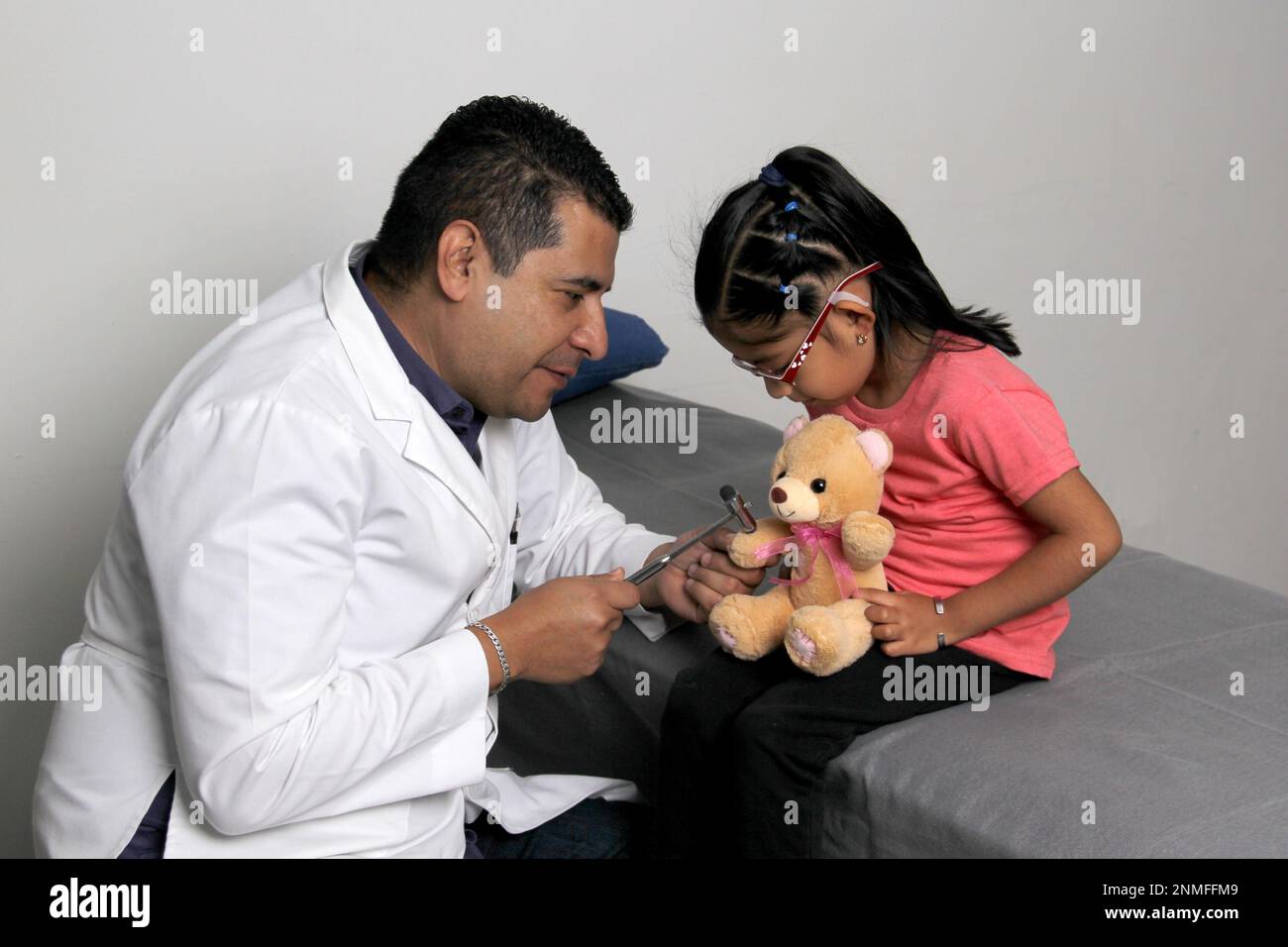 Latino pediatrician doctor checks his girl patient with autism spectrum ...