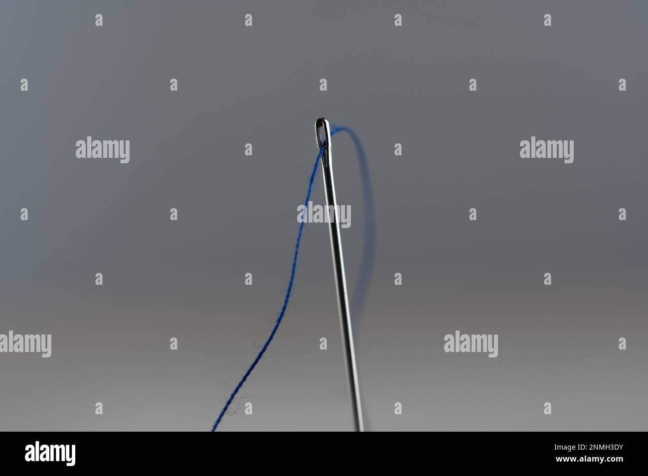 Sewing needle and blue thread against a neutral background Stock Photo ...