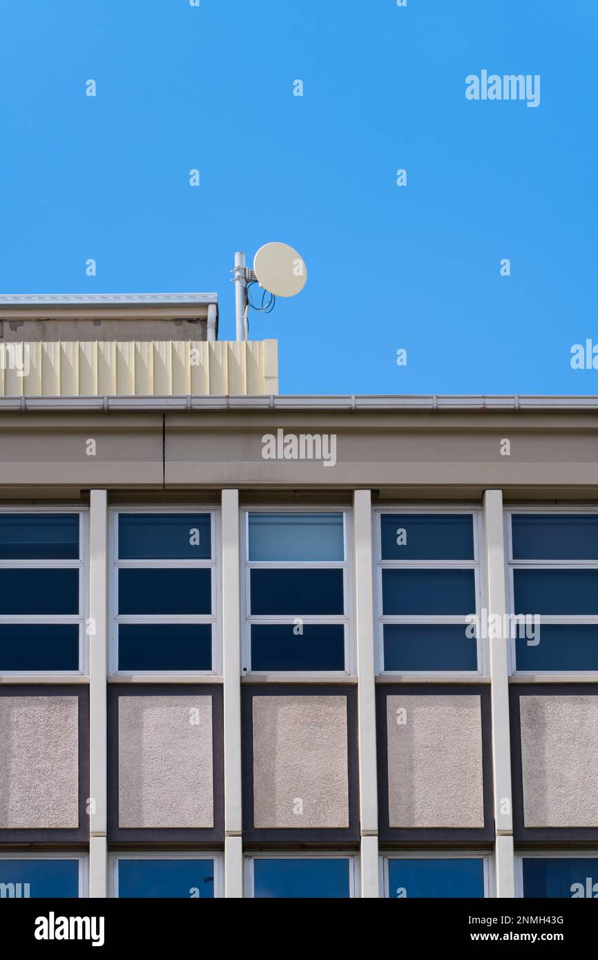 A circular satellite dish sits on the roof of a symmetrical building ...