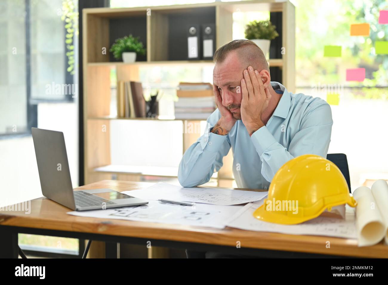 Stressed caucasian engineer man working with blueprints, examining ...