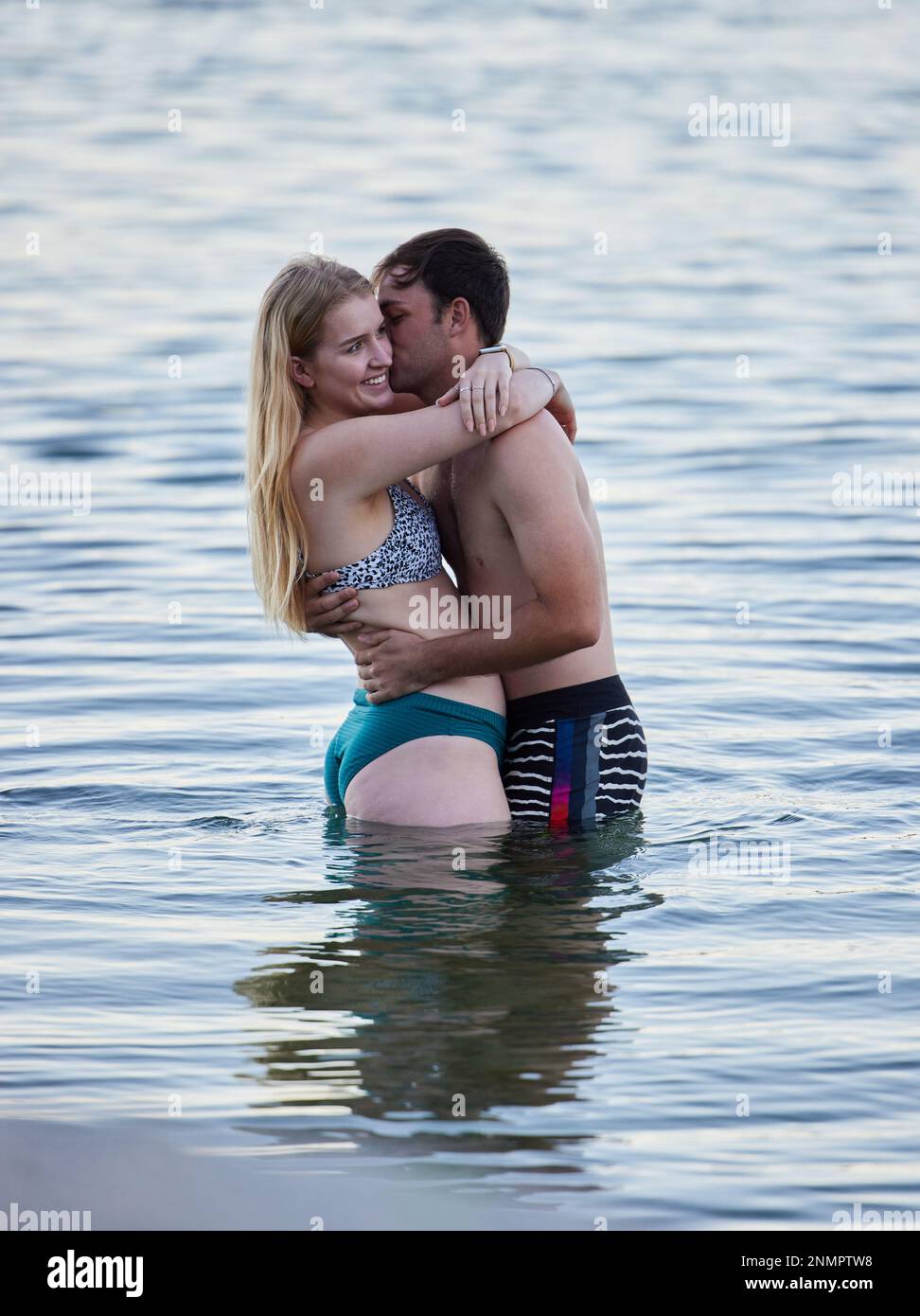 Kiss, hug and couple swimming by the beach for bonding, quality time and holiday by ocean ...