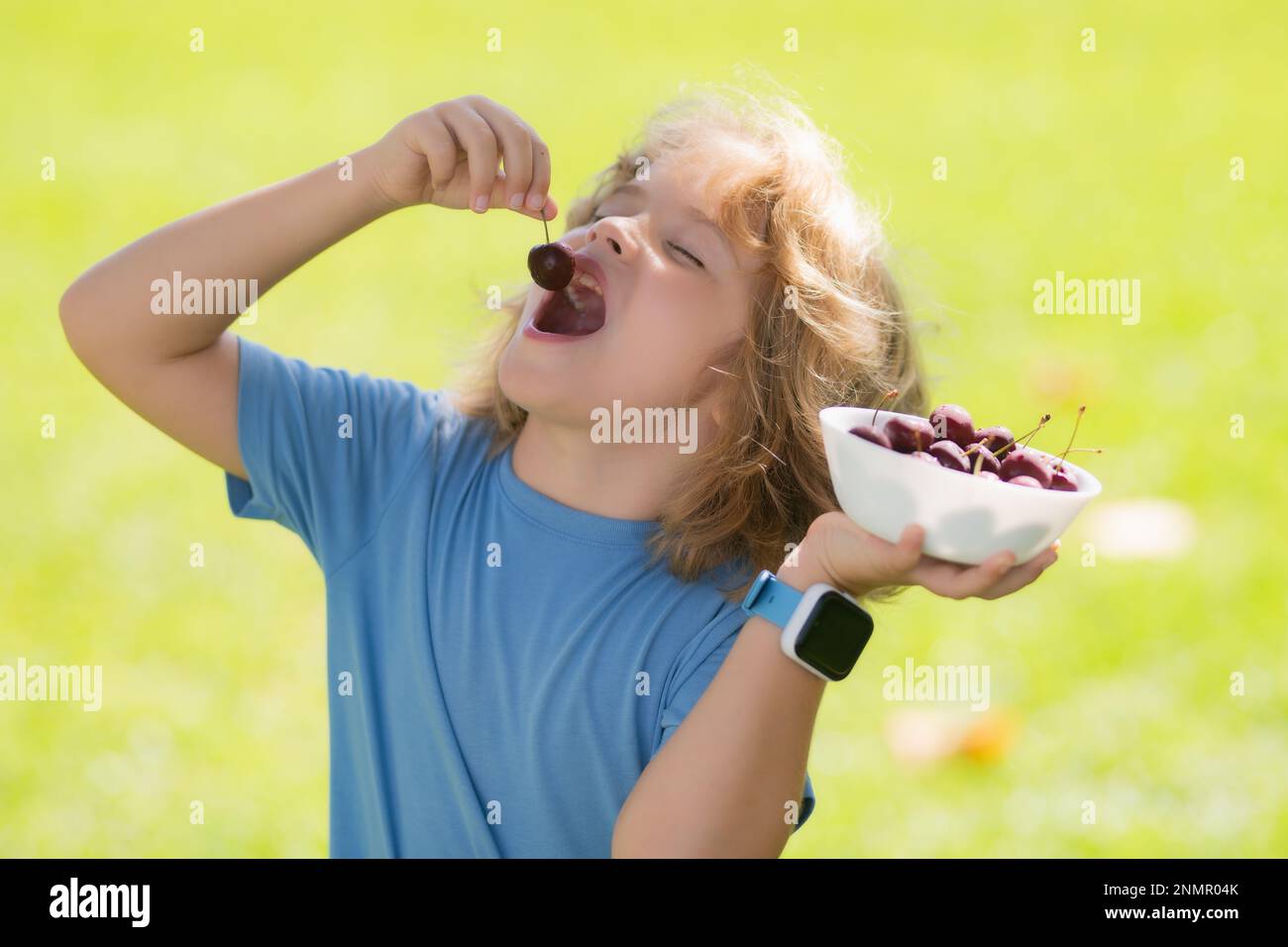 Cherry in kids mouth. Happy little child with cherry outdoors. Kid ...