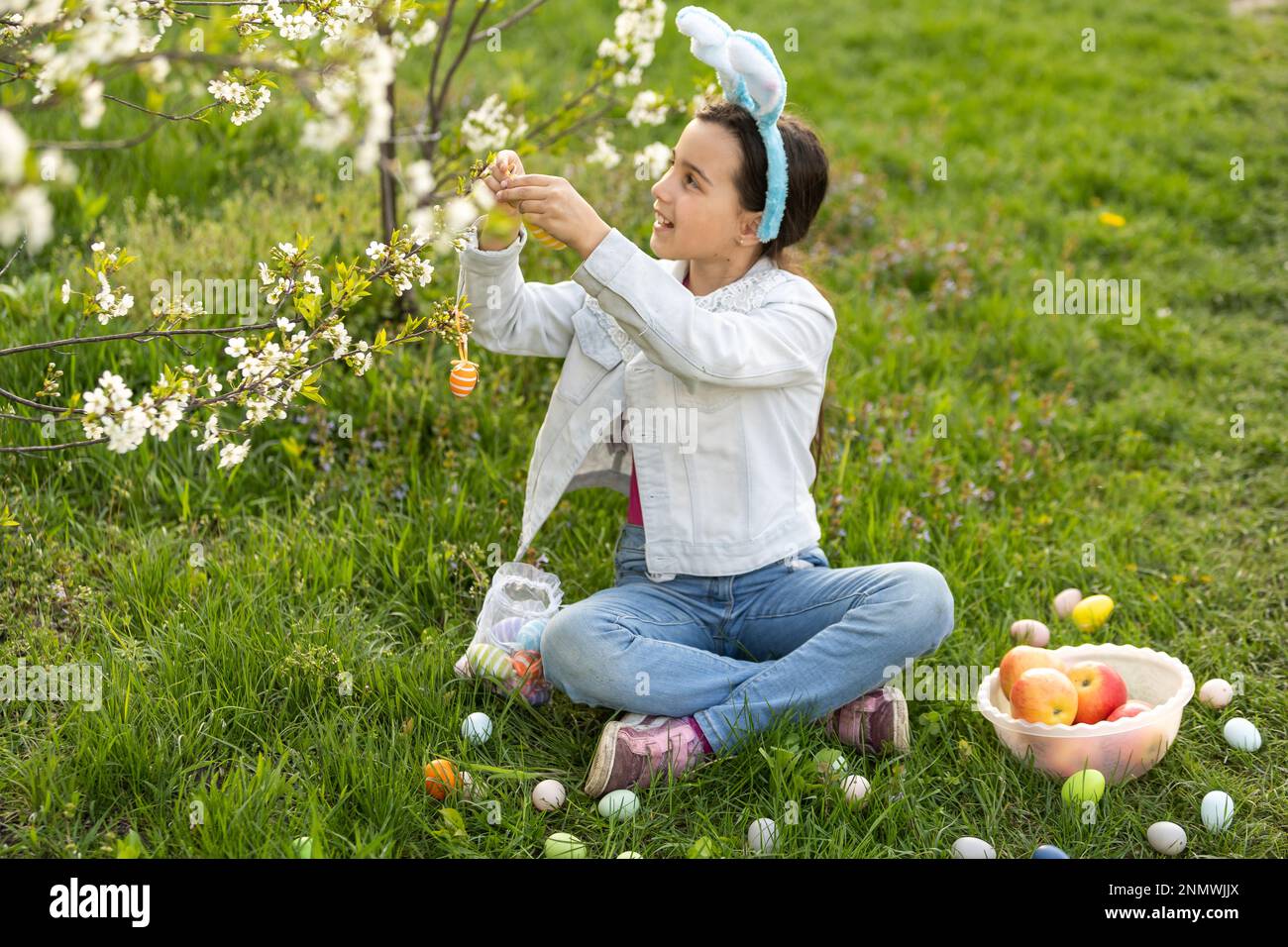 little girl wearing bunny ears with colorful Easter eggs outdoors on ...