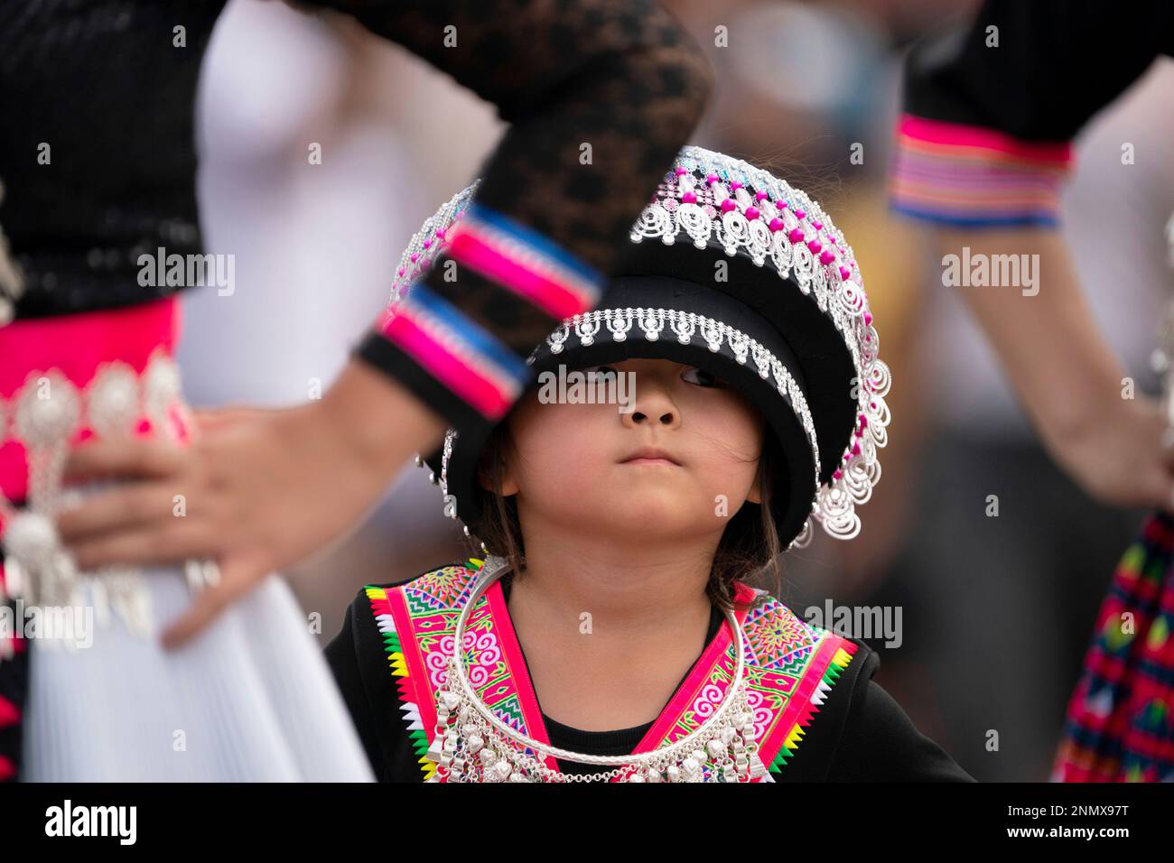 A young participant in traditional Hmong costume walks with older girls ...