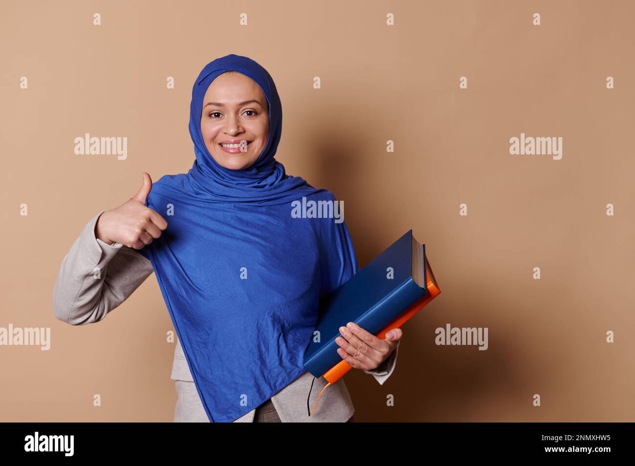 Modern Arabic woman in a blue hijab, smiles and thumbs up, looking at ...