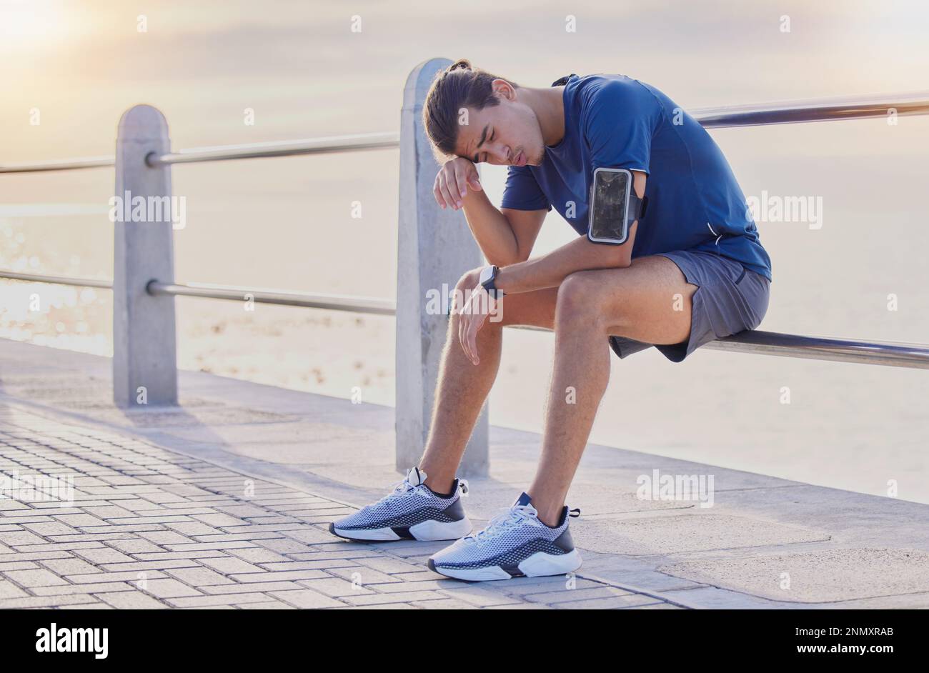 Tired runner man, sitting and beach for workout, health and exercise ...