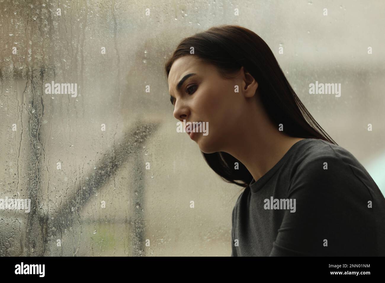 Depressed woman near window on rainy day, space for text Stock Photo ...