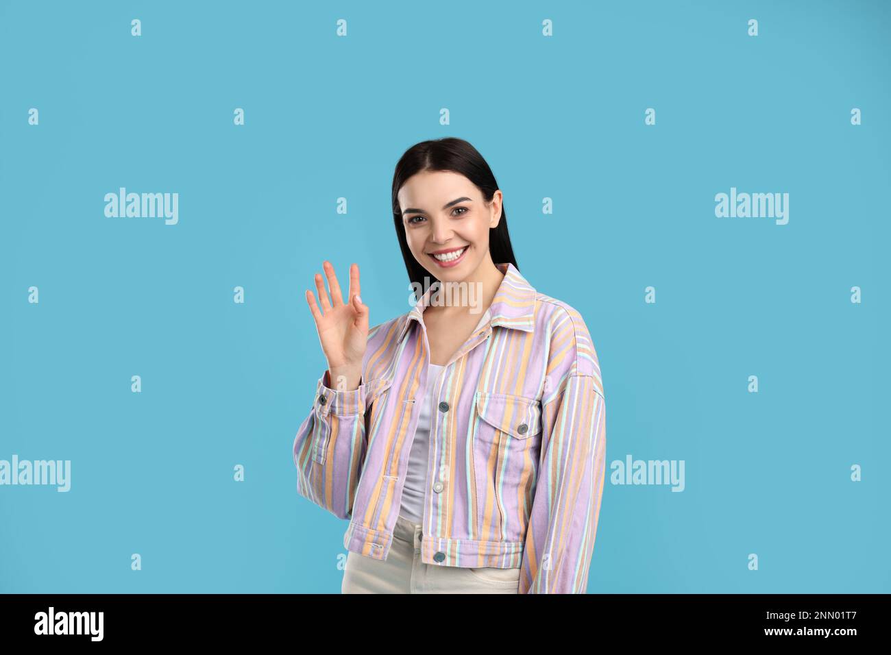 Attractive young woman showing hello gesture on light blue background ...
