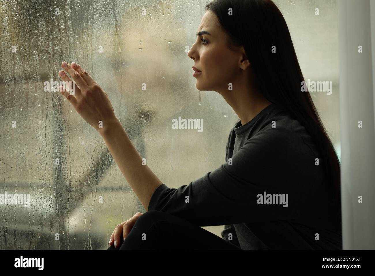 Depressed woman near window on rainy day Stock Photo - Alamy