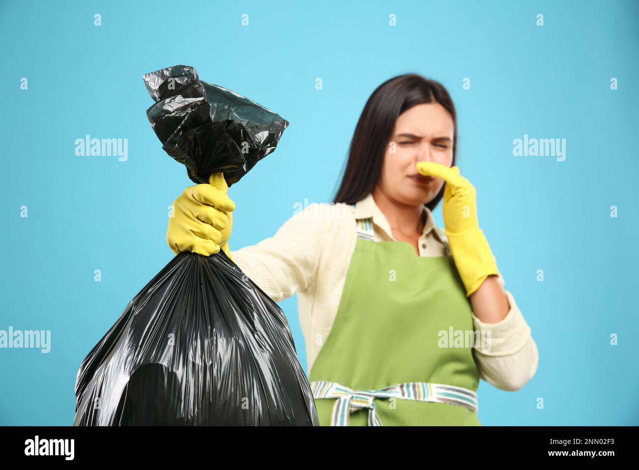 Woman holding full garbage bag against light blue background, focus on ...