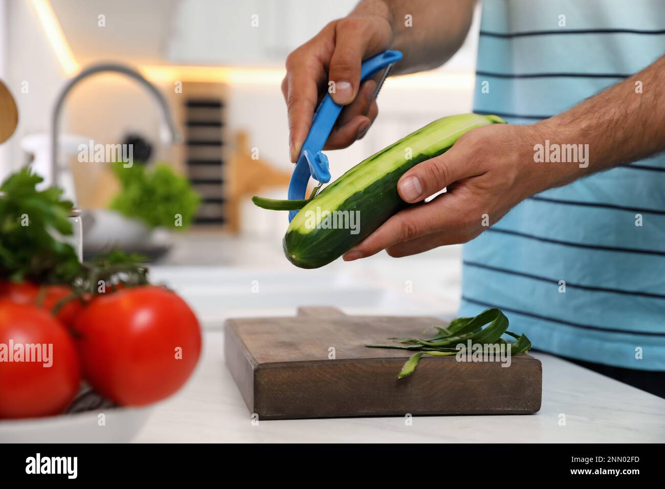 Man peeling cucumber at kitchen counter, closeup. Preparing vegetable ...