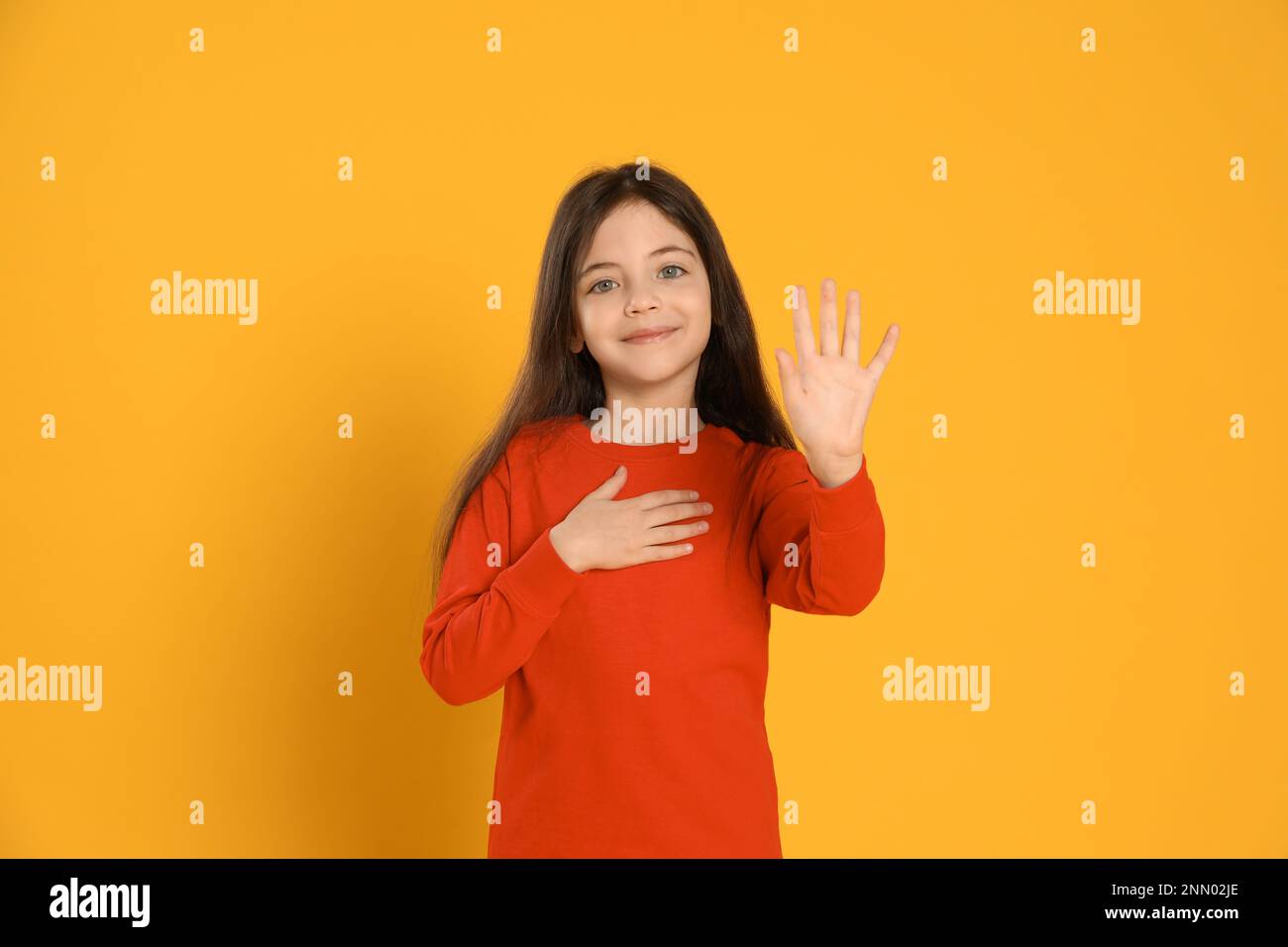 Happy little girl waving to say hello on yellow background Stock Photo ...
