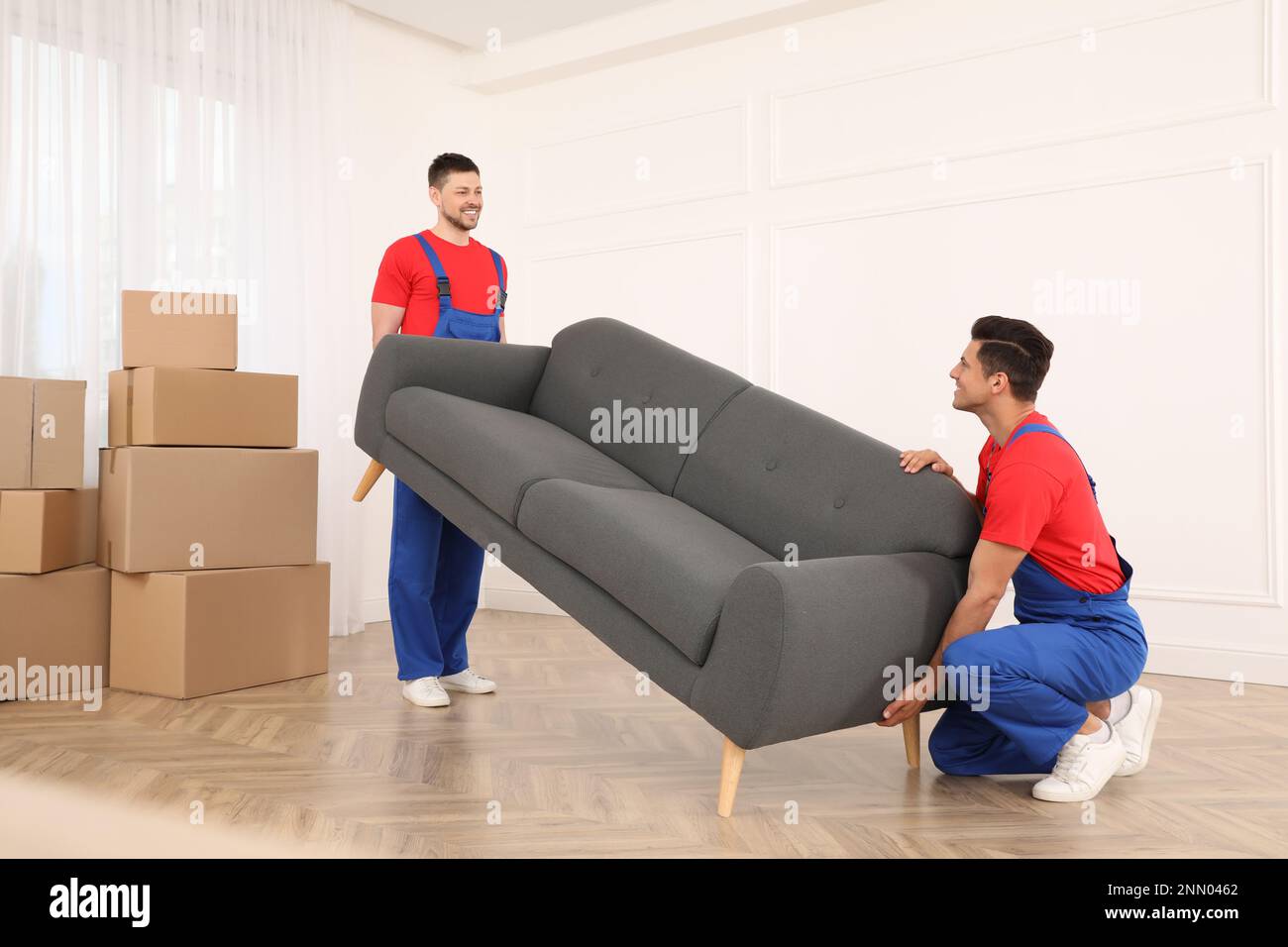 Professional movers carrying sofa in new house Stock Photo - Alamy