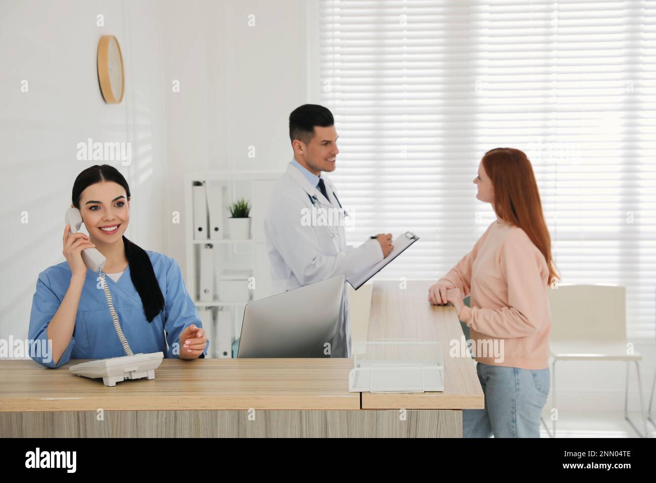 Receptionist talking on phone while doctor working with patient in ...