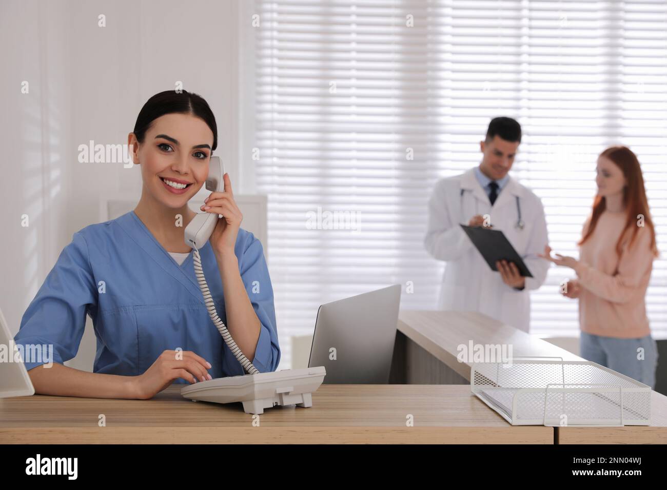 Receptionist talking on phone while doctor working with patient in ...