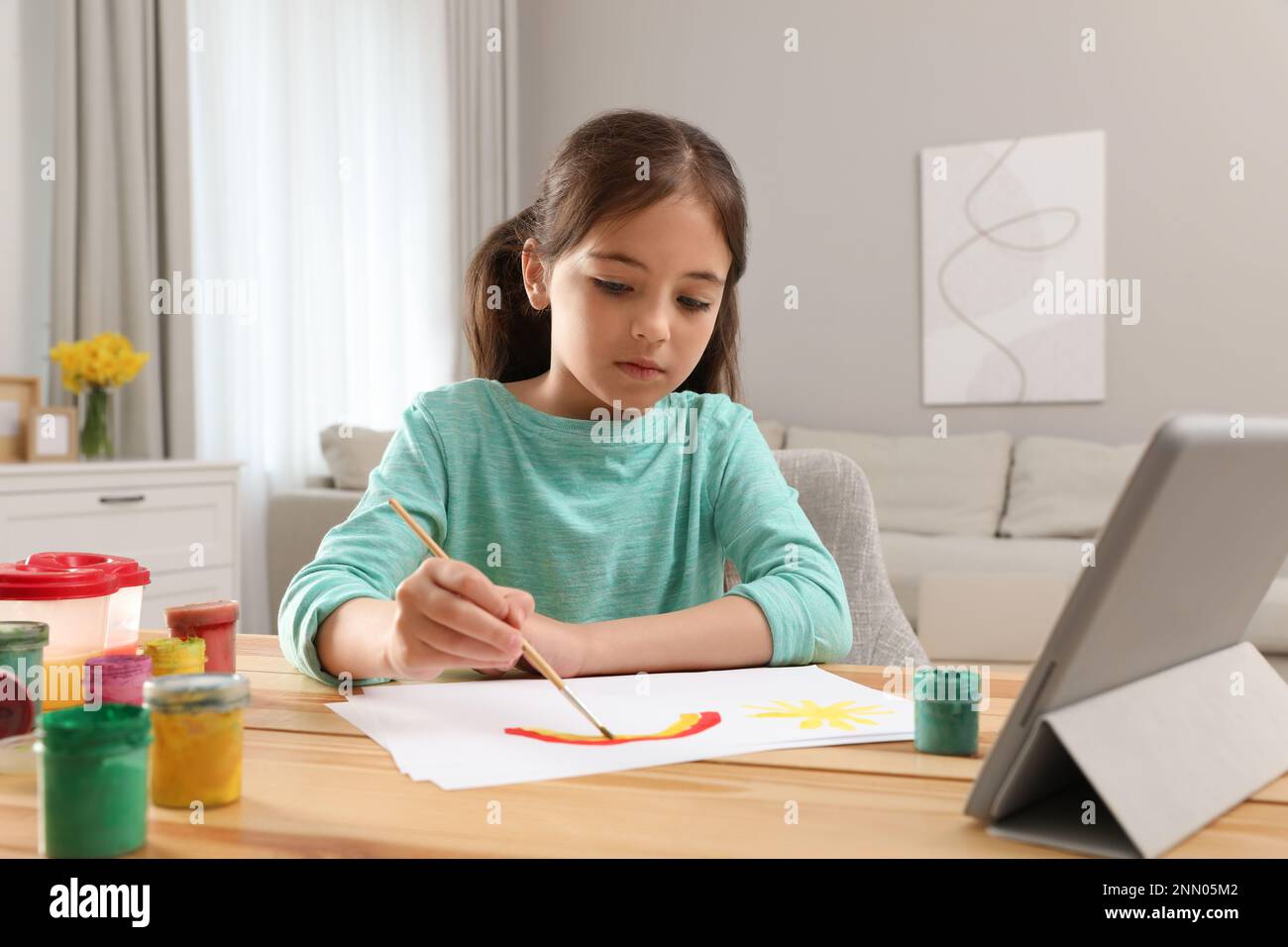 Little girl drawing on paper with paints at online lesson indoors ...