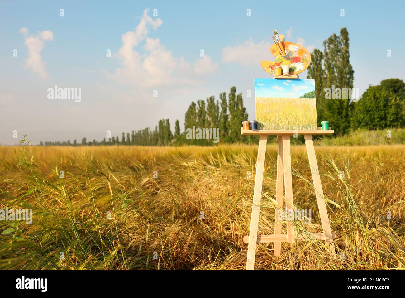 Wooden easel with beautiful picture and painting equipment in field ...