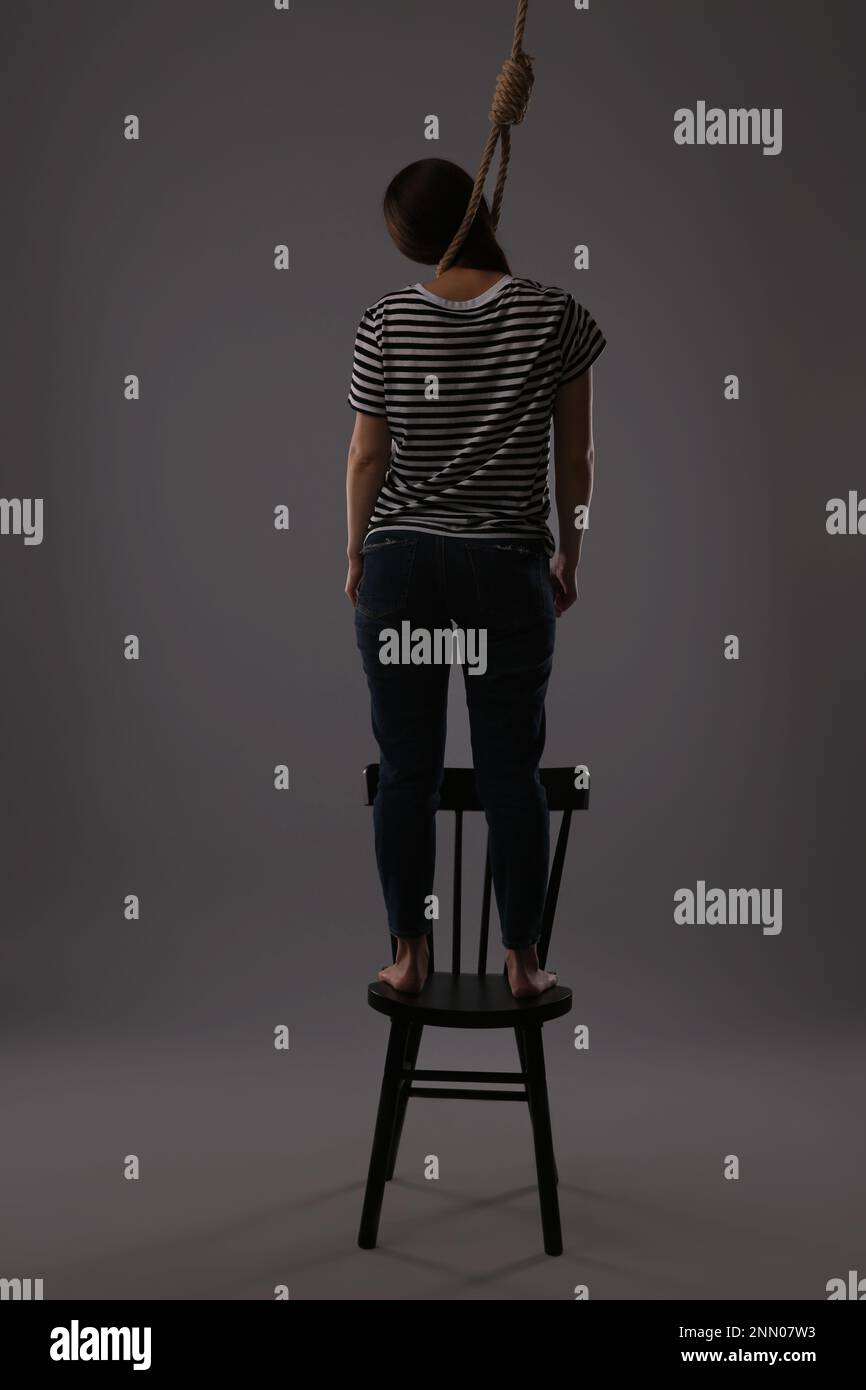 Woman with rope noose standing on chair against grey background, back ...